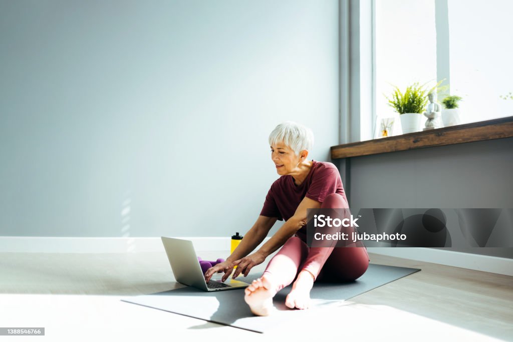 Mature Woman Exercising At Home Watching Virtual Exercise Class On