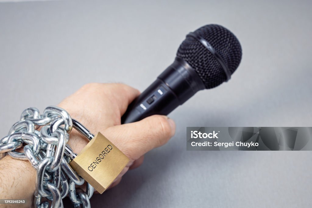 Hand Holding Microphone Tied With Chains And Lock On Grey Surface Free