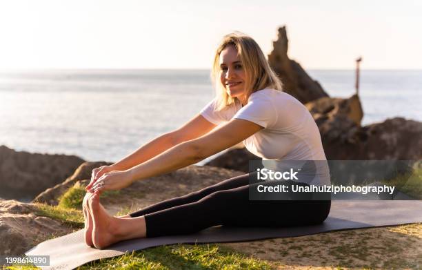 A Blonde Woman Doing Yoga Exercises In Nature By The Sea Stretching