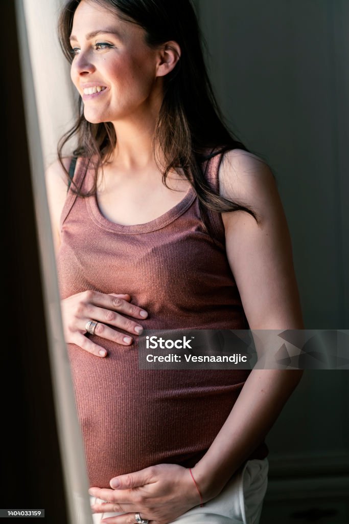 Happy Middle Aged Pregnant Woman At Home Looking Outside The Window