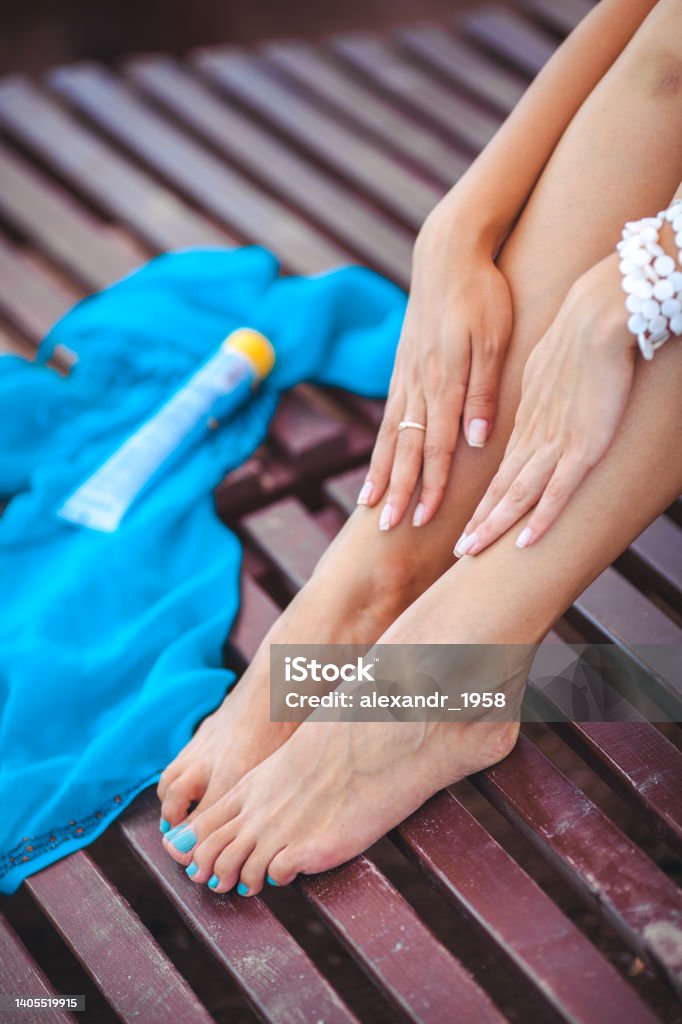 Young Woman Applying Sunscreen To Her Legs While Sitting On A Sun