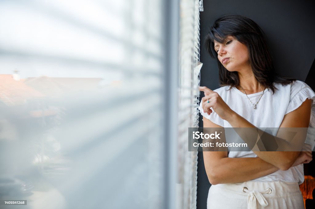 Annoyed Woman Standing By The Window Arms Crossed Peeking Outside