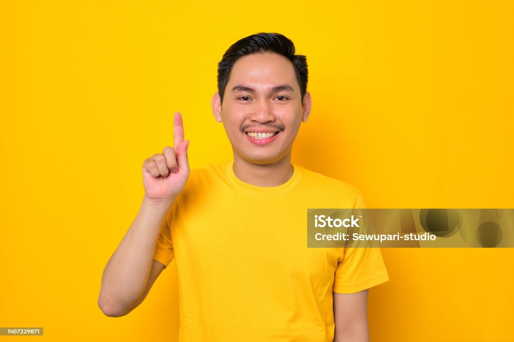 Excited Young Asian Man In Casual Tshirt Pointing Finger Up Having An