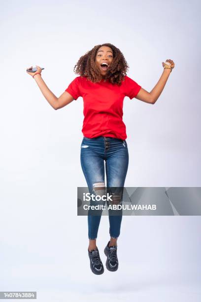 Wanita Muda Afrika Yang Bahagia Melompat Kegirangan Memegang Teleponnya ... Wanita Muda Afrika Yang Bahagia Melompat Kegirangan Memegang Teleponnya ...