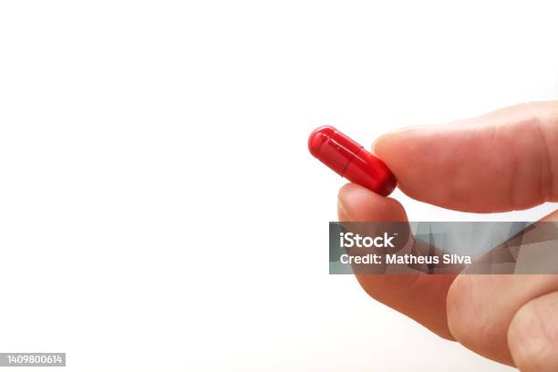 Memegang Kapsul Obat Merah Dengan Latar Belakang Putih Dan Ruang Salin