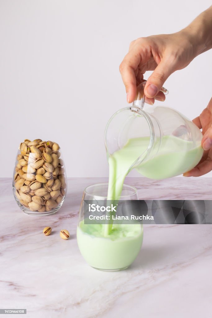Sebuah Tangan Menuangkan Susu Pistachio Dari Botol Kaca Ke Dalam Gelas Foto Stok Unduh Gambar