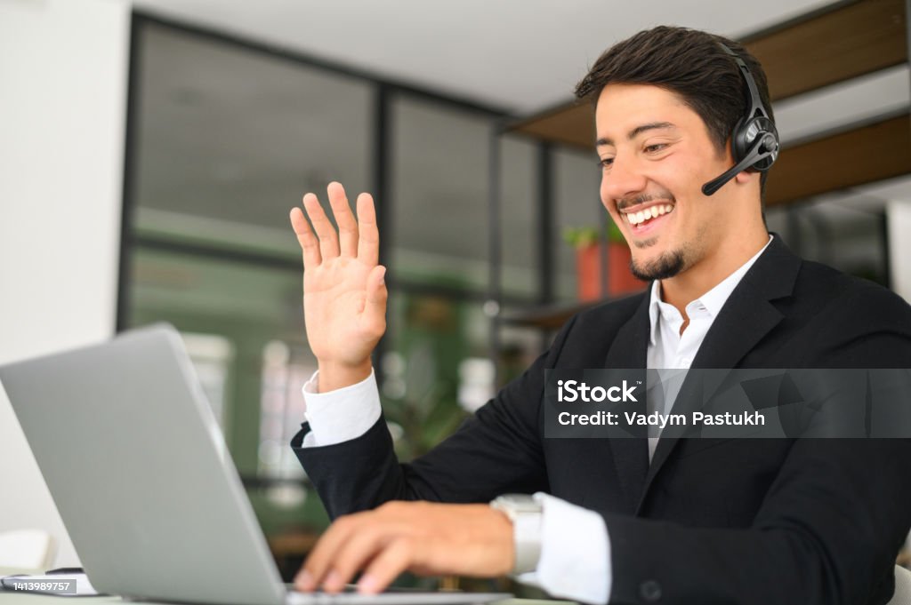 Handsome Young Hispanic Businessman In Smart Formal Business Wear Using Headset And Laptop For