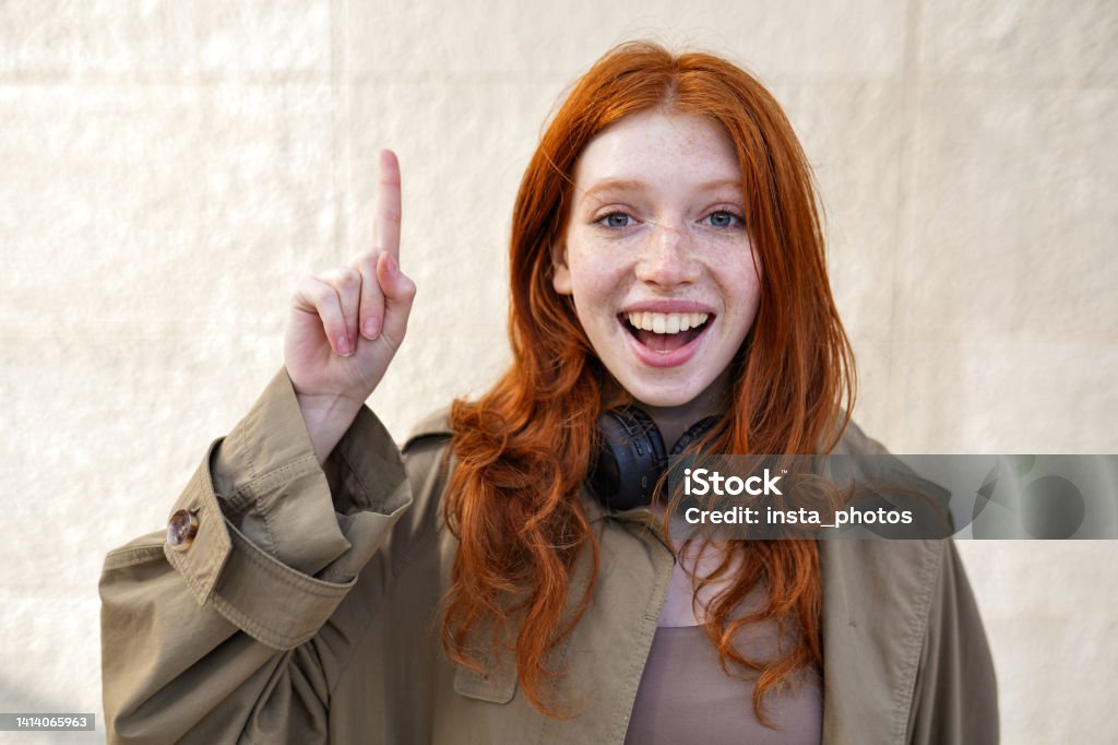 Happy Teen Redhead Girl Standing On Urban Wall Background Pointing Up