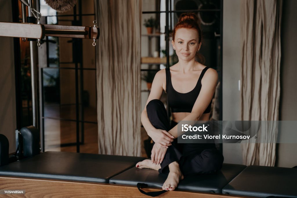 Beautiful Young Pilates Trainer Sitting With Arms Around Legs In Calm