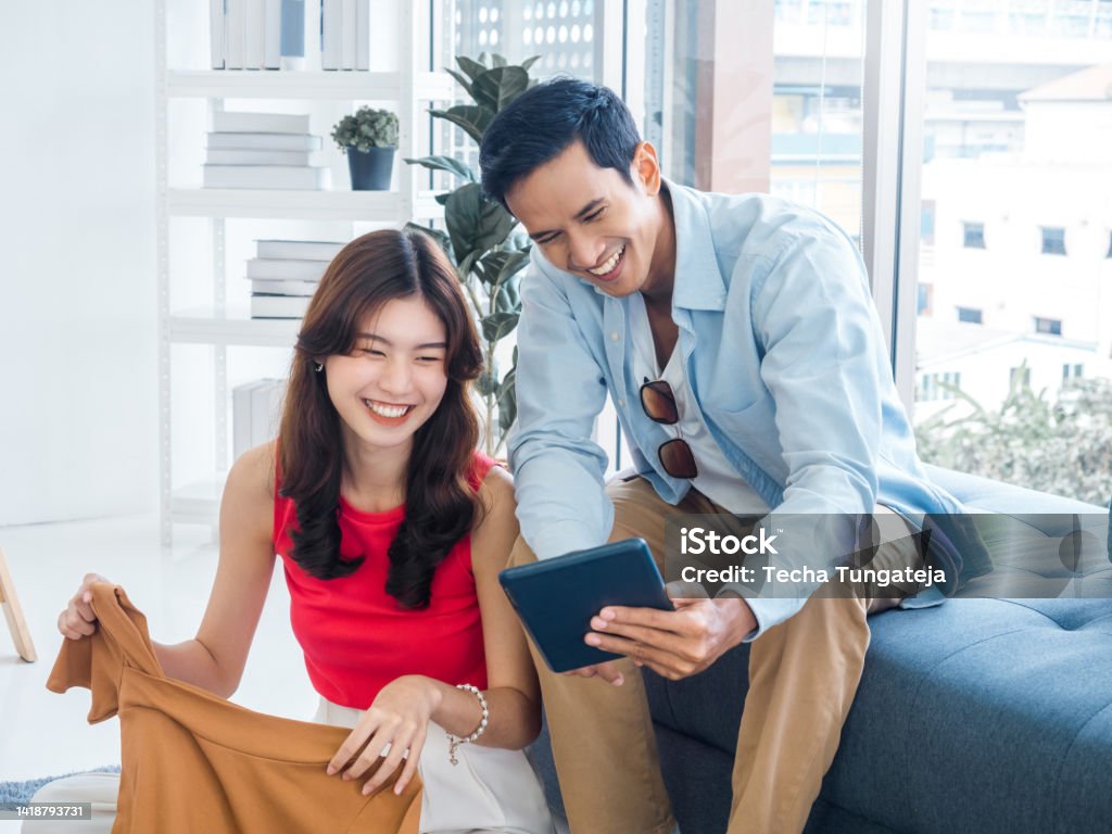 Happy Handsome Asian Man And Young Beautiful Woman Laughing Together While Looking At Tablet