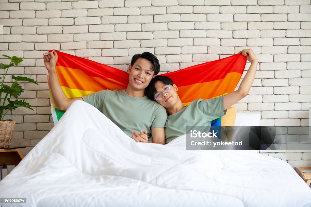 Happy Asian Gay Couple Talking Together And Relaxing At Home On Bed