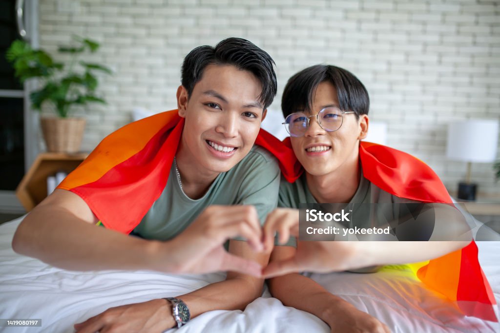 Happy Asian Gay Couple Talking Together And Relaxing At Home On Bed