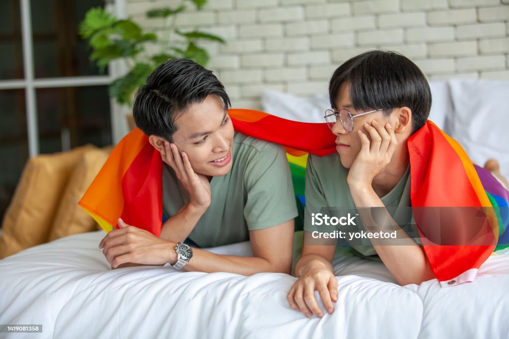 Happy Asian Gay Couple Talking Together And Relaxing At Home On Bed