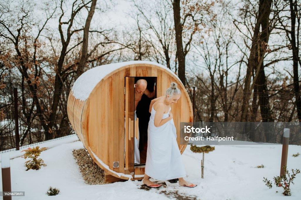 Senior Woman In Towel With Her Husband Coming Out From Outdoor Sauna
