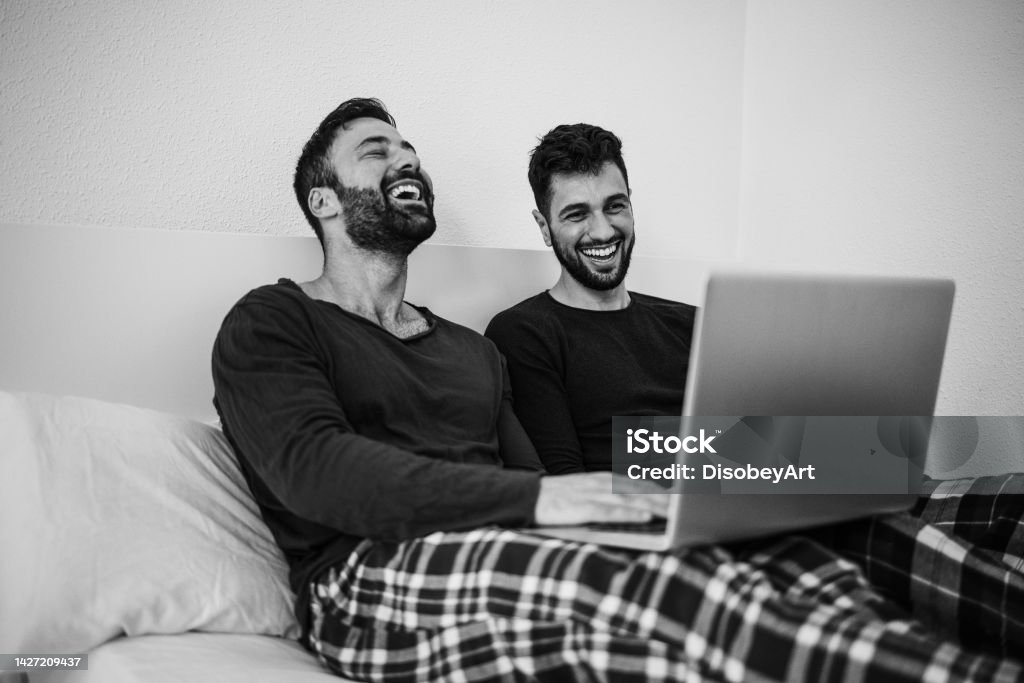 Happy Gay Men Couple Using Laptop Computer In Bed At Home Focus On