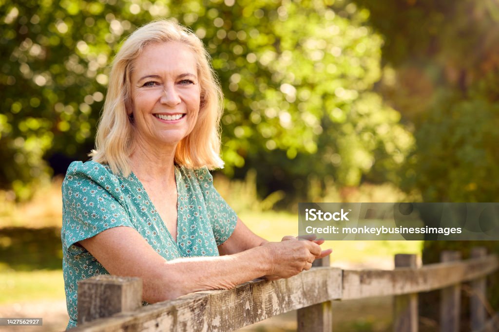 Portrait Of Casually Dressed Mature Or Senior Woman Leaning On Fence On
