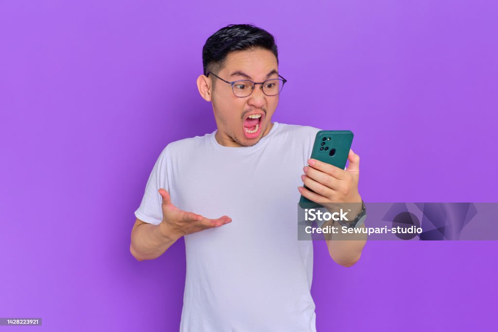 Shocked Young Asian Man In White Tshirt Looking At Smartphone With Wow