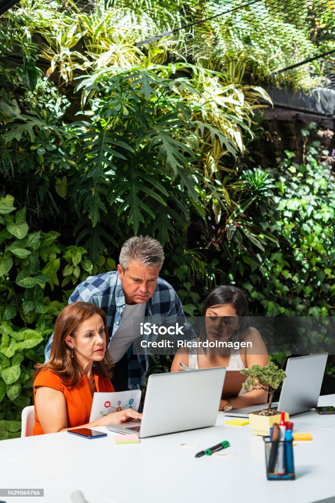 Three Coworkers Two Women And An Older Man Are At One Of The Office Desks Discussing Work Issues