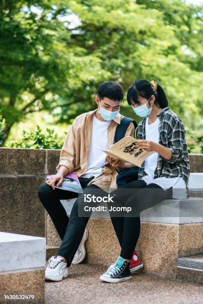 Siswa Lakilaki Dan Perempuan Yang Mengenakan Topeng Duduk Dan Membaca