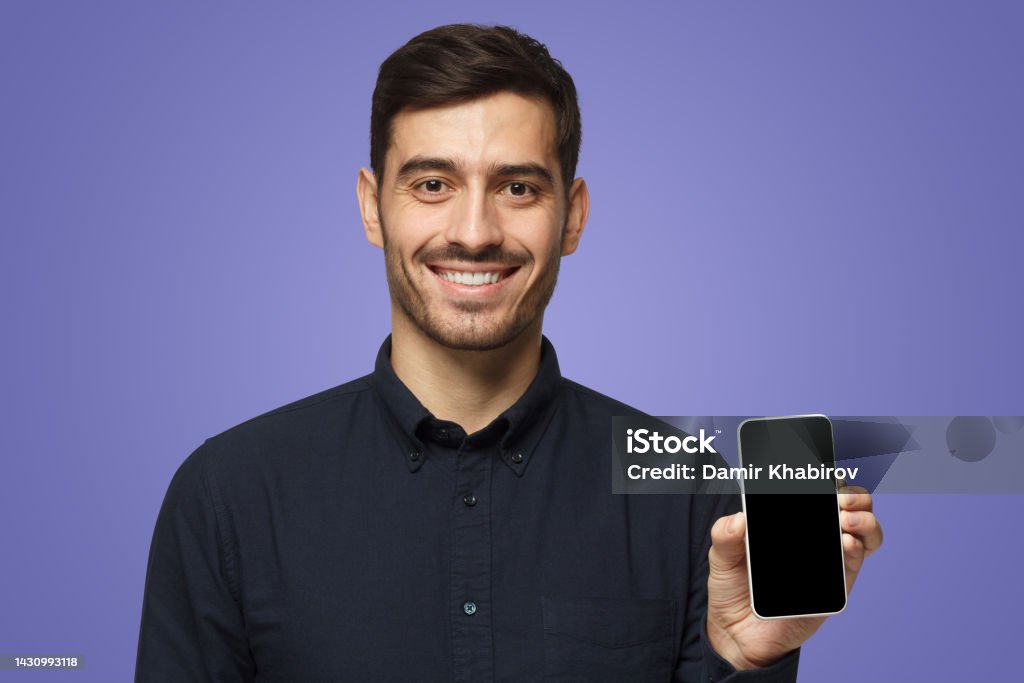 Smiling Handsome Young Man Holding Smartphone With Blank Screen