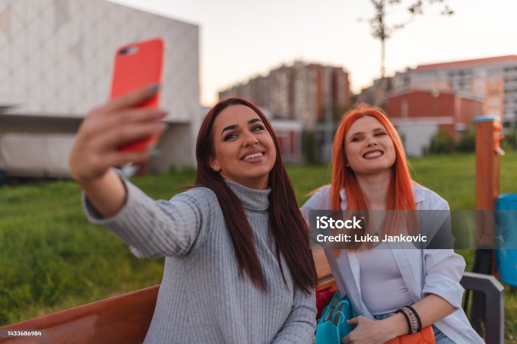 Two Redheaded Women Taking Selfies While Sitting On A Park Bench