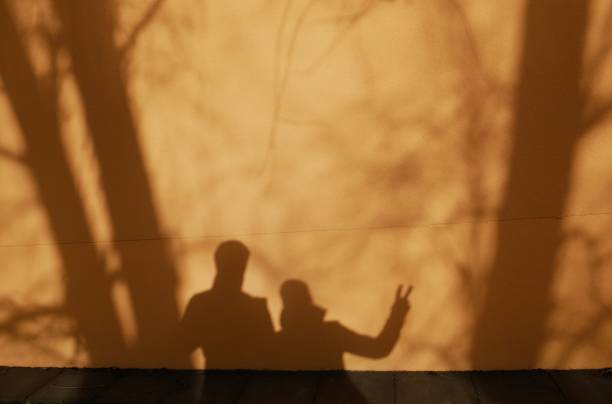Free Stock Photo of Two people leaning against a wall, casting long ...