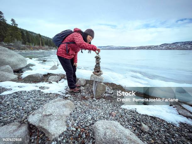 Mature Asian Woman Carefully Dismantling Rock Cairn At Frozen ... Mature Asian Woman Carefully Dismantling Rock Cairn At Frozen ...