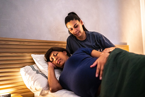 Mid Adult Woman Taking Care Of Her Pregnant Wife While Shes Sleeping In The Bedroom At Home