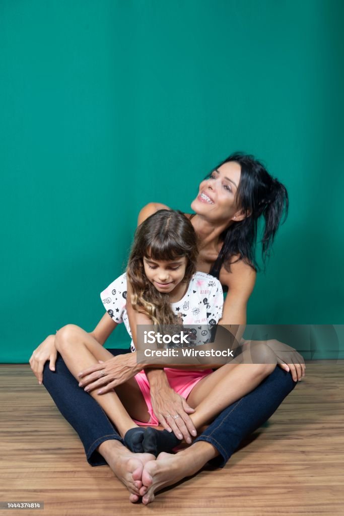 Portrait Of A Happy Mother And Daughter Sitting On Wooden Floor Against