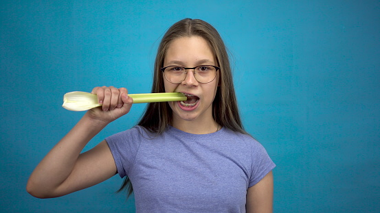 Teenage Girl With Braces On Her Teeth Eats Celery On A Blue Background