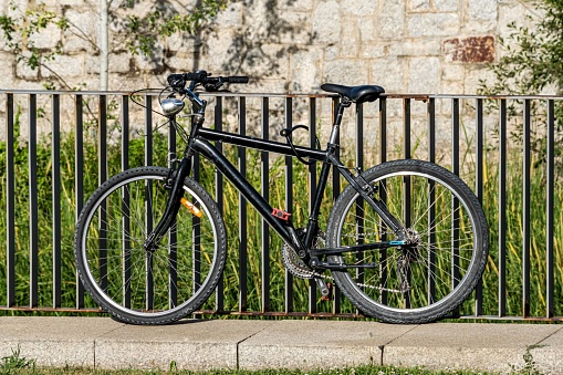 Black Bicycle Parked And Chained To A Fence In A Park With Green ... Black Bicycle Parked And Chained To A Fence In A Park With Green ...