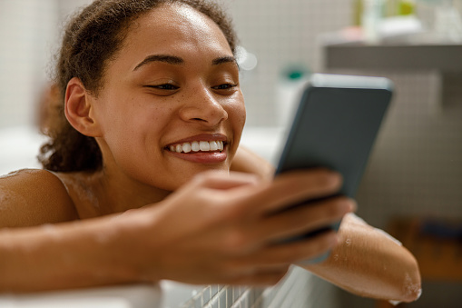Smiling Afro American Woman Is Using Smartphone When Taking A Bath At