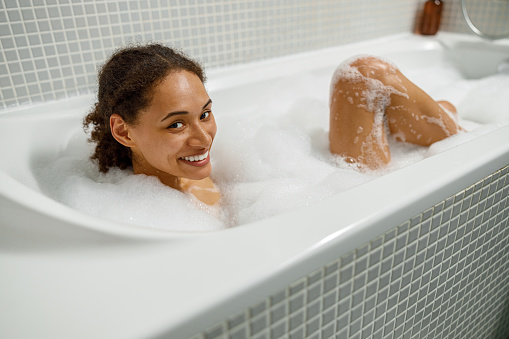 Smiling Afro American Woman Takes Bubble Bath In Bathtub Spa Wellness