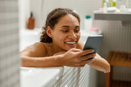 Smiling Afro American Woman Is Using Smartphone When Taking A Bath At