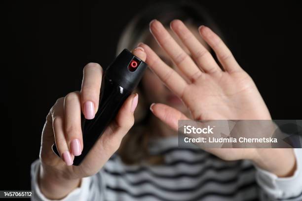 Young Woman Using Pepper Spray Against Black Background Focus On Hands