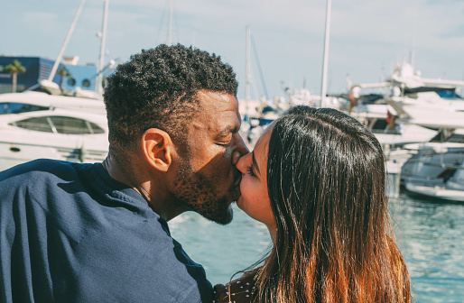 Close Up Of Interracial Couple Kissing At The Port With Boats