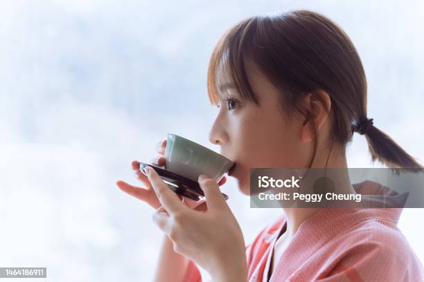 冬の間雪の中の山の自然の景色を望む部屋でくつろぎながら熱いお茶を飲む着物を着たアジアの若い女性 女性のストックフォトや画像を多数ご用意