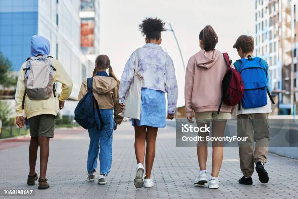 Rear View Of Youthful Interracial Pupils Walking Down Street Stock