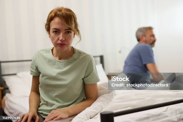 Couple Sitting On Different Sides Of Bed Not Talking After Argument