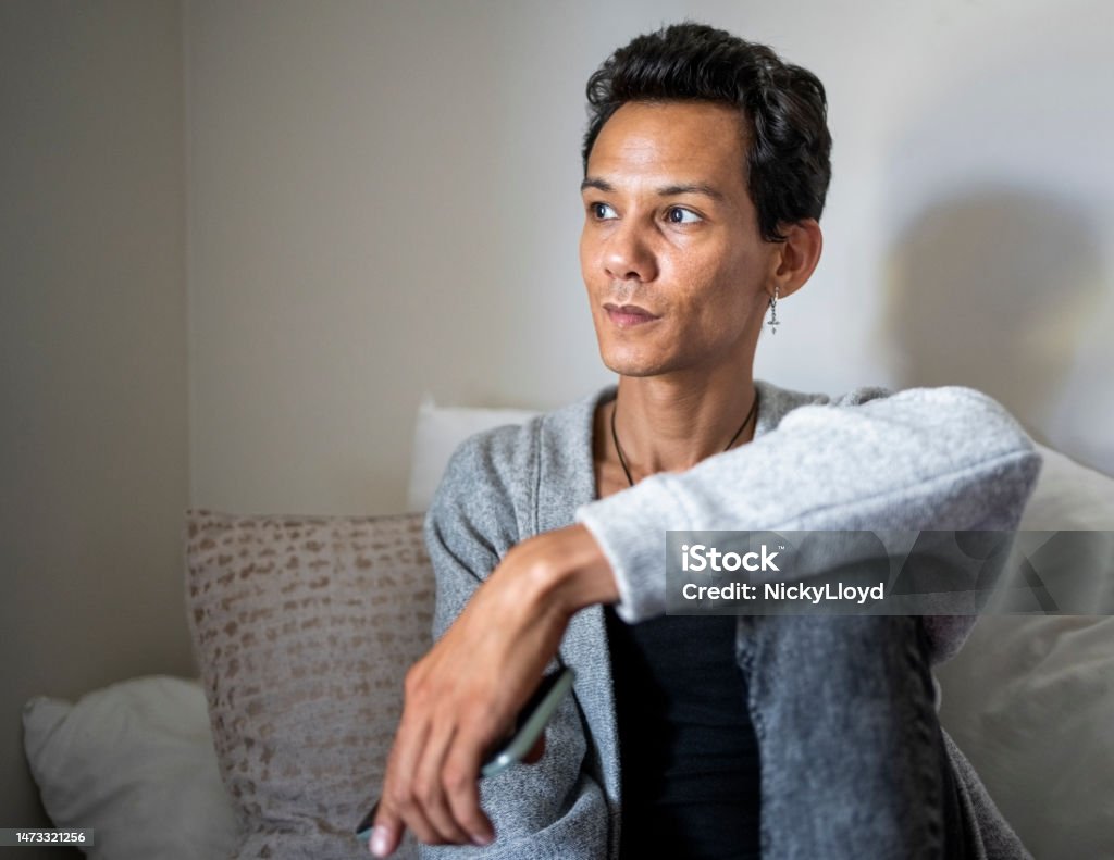 Gender Fluid Person Looking Away And Thinking Sitting On Sofa At Home