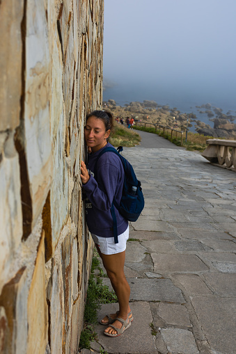 The Girl Pressed Herself Against The Stone Wall Behind A Cute View Of The Ocean And The Path To