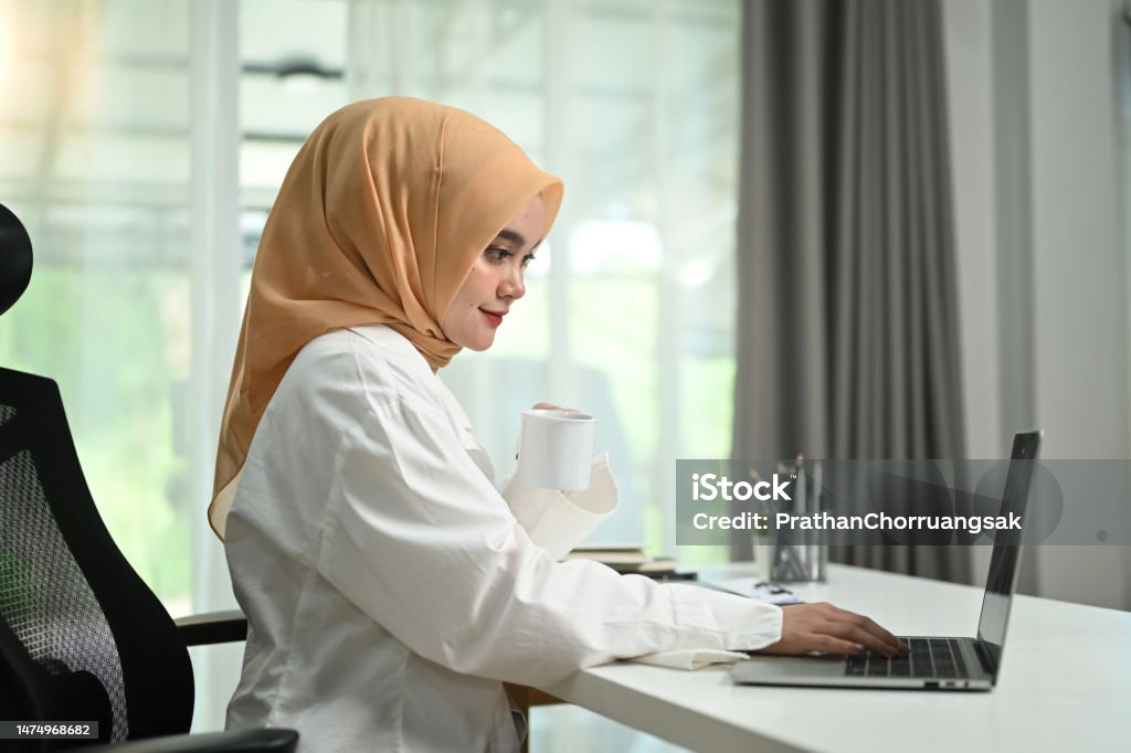 Tampak Samping Wanita Pekerja Muda Cantik Berhijab Memegang Secangkir Kopi Dan Menggunakan