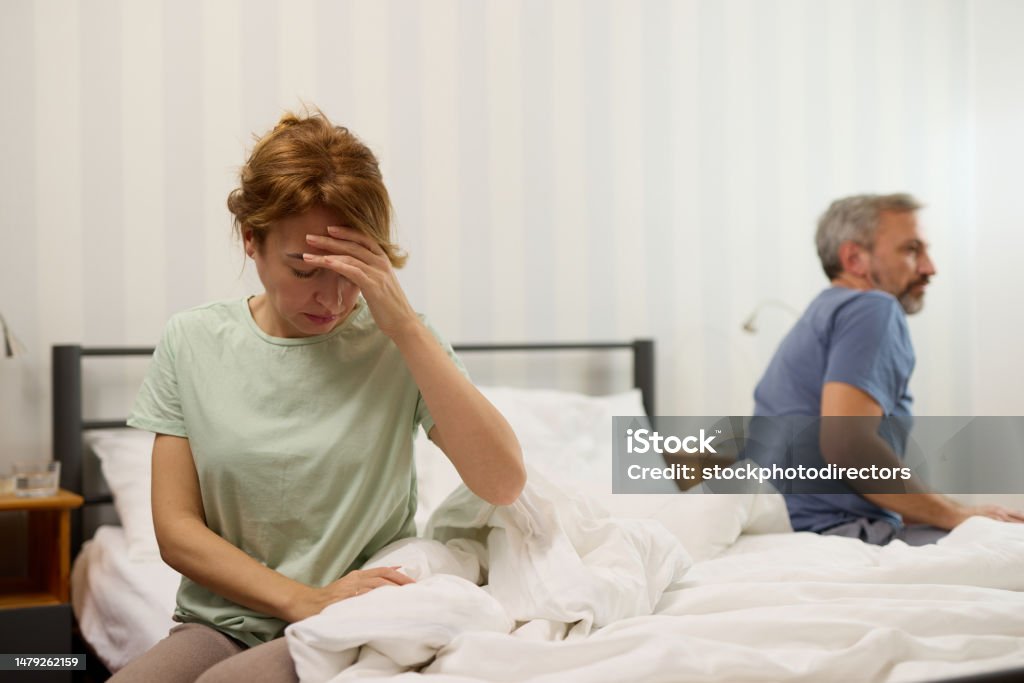 Couple Sitting On Different Sides Of Bed Not Talking After Argument