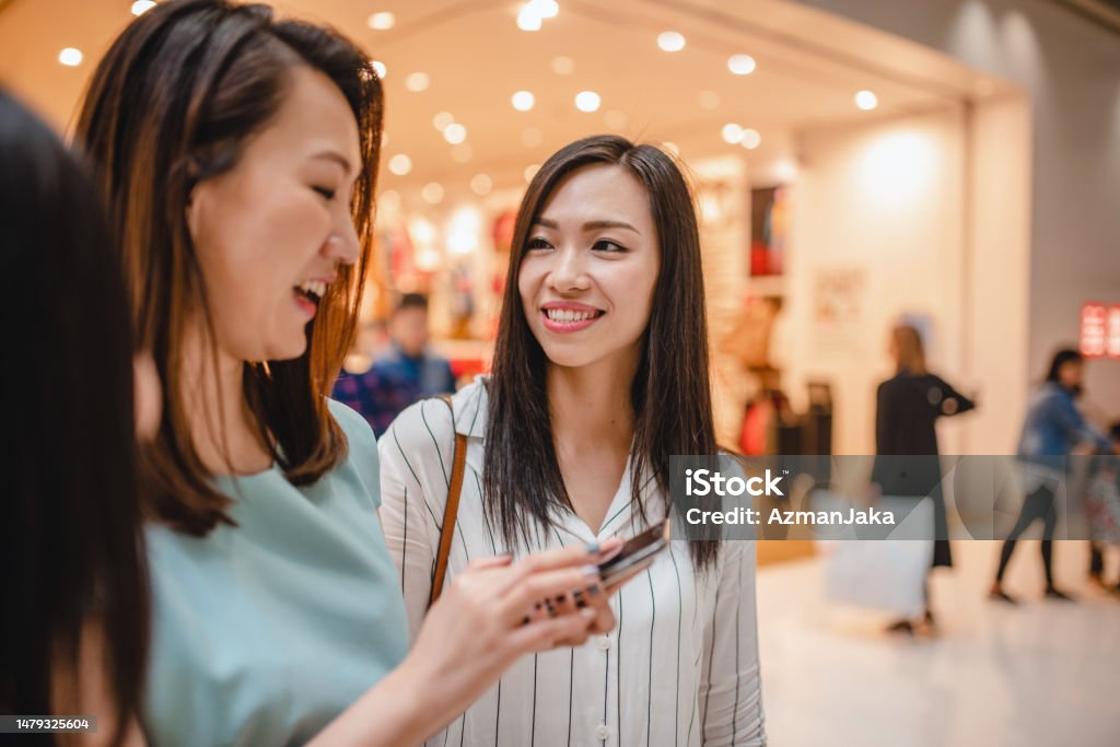 Asiatische Frau Die Ihren Freund Ansieht Der Im Einkaufszentrum Ein Smartphone Hält Stockfoto