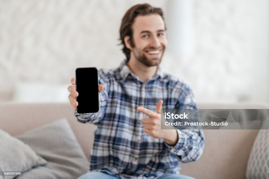 Satisfied Millennial Caucasian Male With Stubble Sit On Sofa Pointing