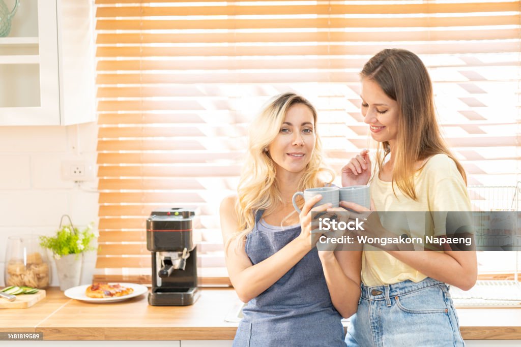 Happy Lesbian Couple Holding Cups Of Coffee In Kitchen Couple Of