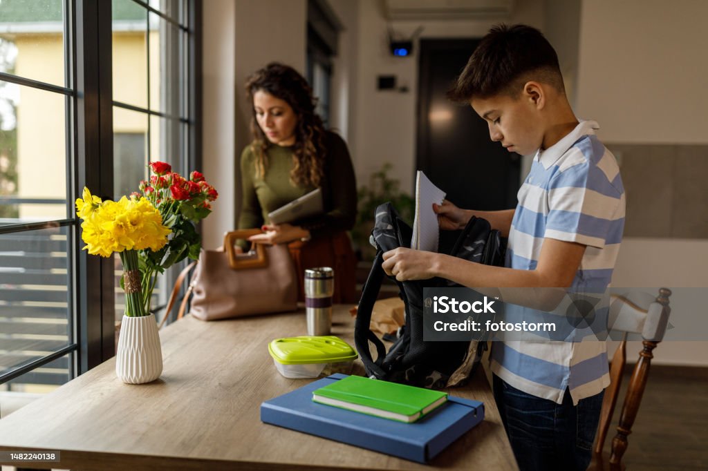 Teenage Boy Packing His School Bag While His Mother Is Preparing To Go ... Teenage Boy Packing His School Bag While His Mother Is Preparing To Go ...