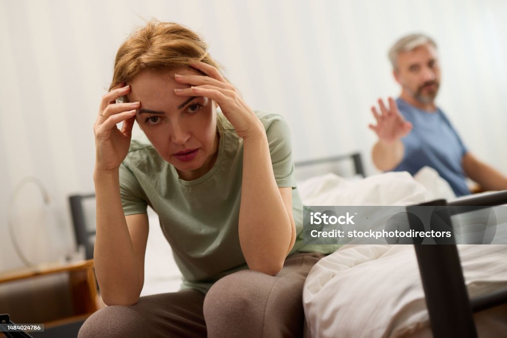Couple Sitting On Different Sides Of Bed Not Talking After Argument