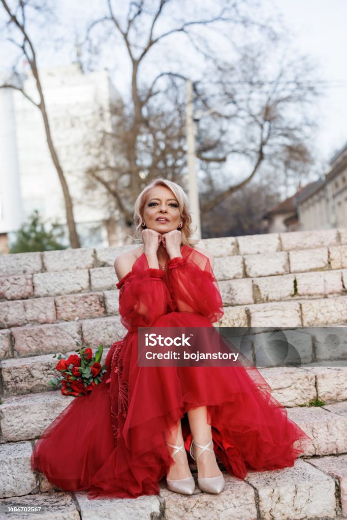Schöne Reife Frau Im Roten Kleid Mit Strauß Roter Rosen Sitzt Auf Der ... Schöne Reife Frau Im Roten Kleid Mit Strauß Roter Rosen Sitzt Auf Der ...
