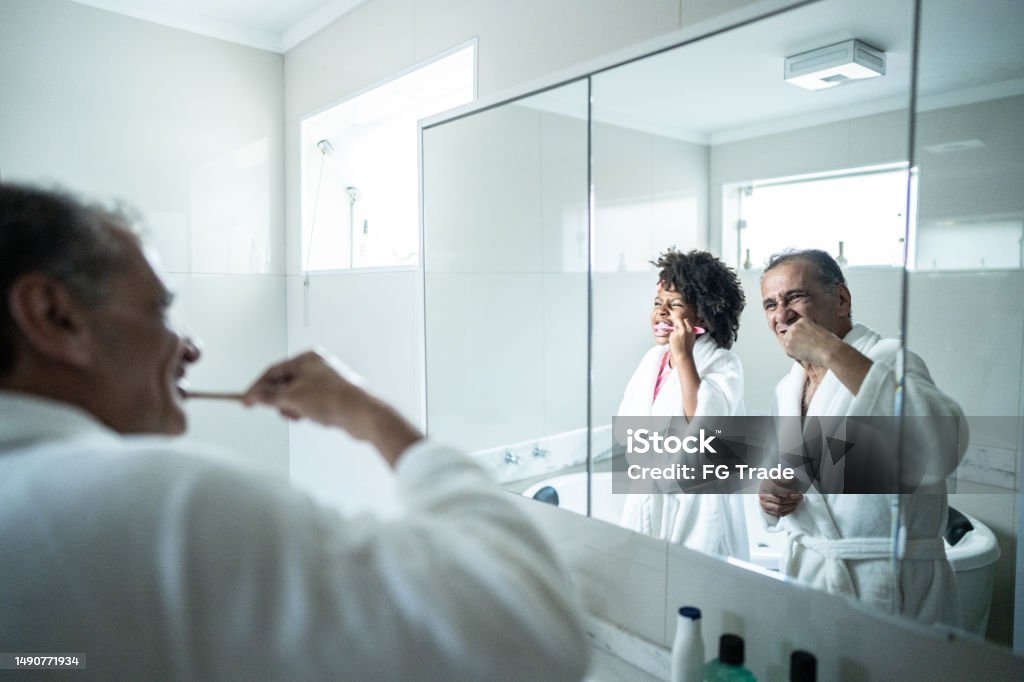 Senior Man Brushing Teeth With Her Granddaughter On The Bathroom At